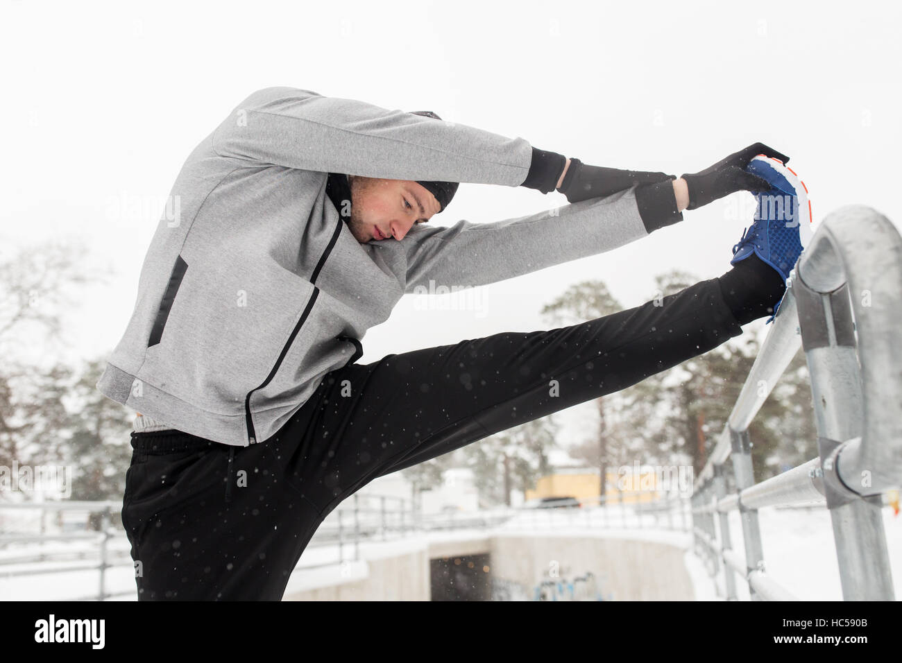 sports man stretching leg at fence in winter Stock Photo - Alamy