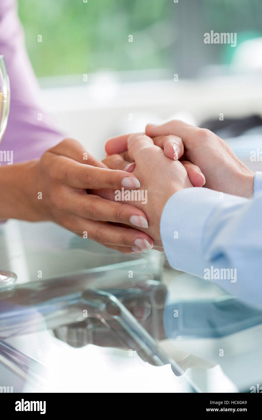 Two people sitting on a table holding hands for comfort Stock Photo - Alamy