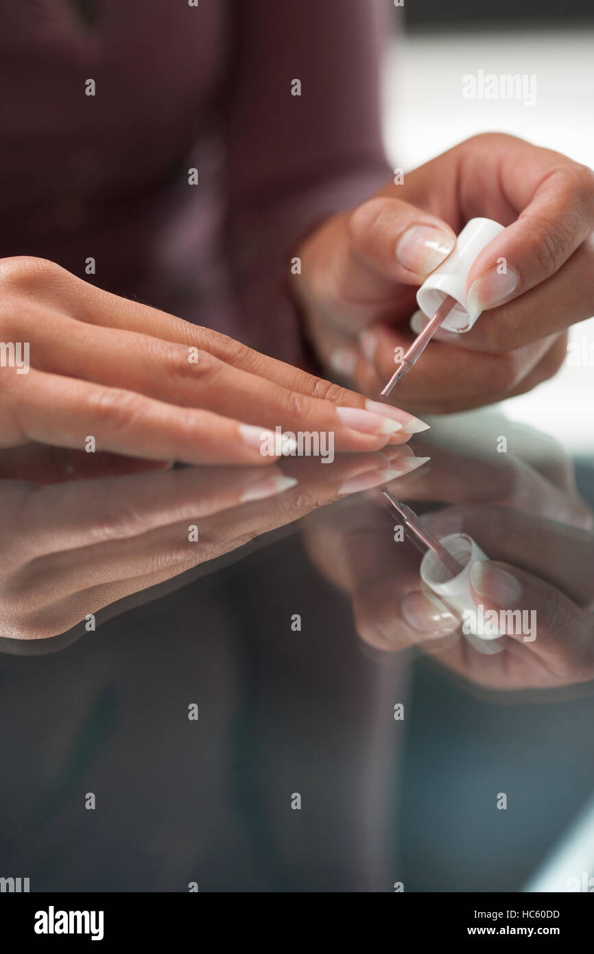 young woman applying pearl tinted nail polish on her nails carefully ...