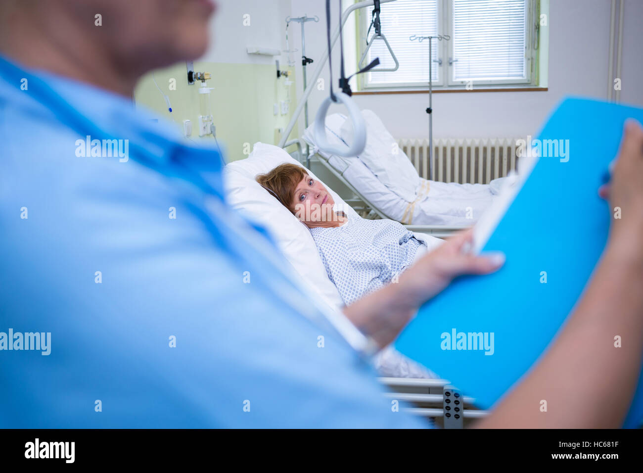 Nurse holding file while senior patient lying on bed in background ...