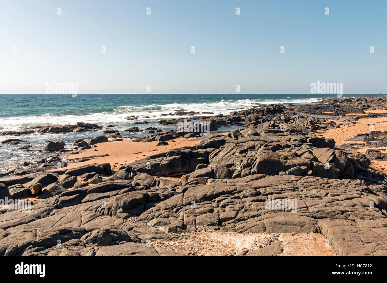 Beach sand rocks ocean and waves against blue skyline in South Africa ...