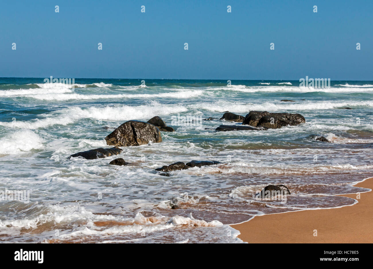 Beach sand rocks ocean and waves against blue skyline in South Africa ...