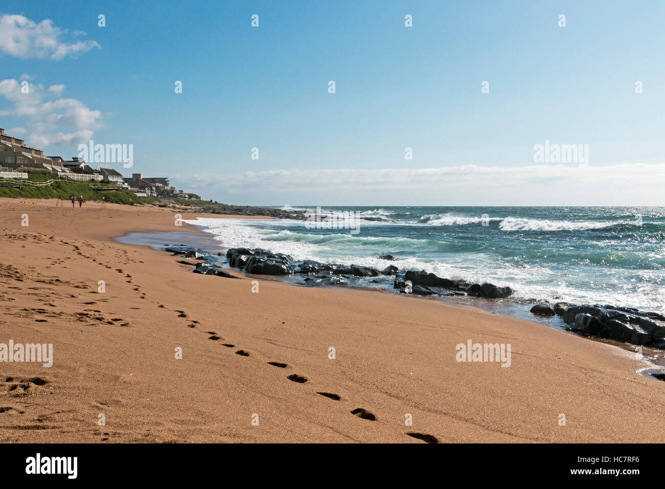 Beach sand rocks ocean and waves against residential buildings and blue ...
