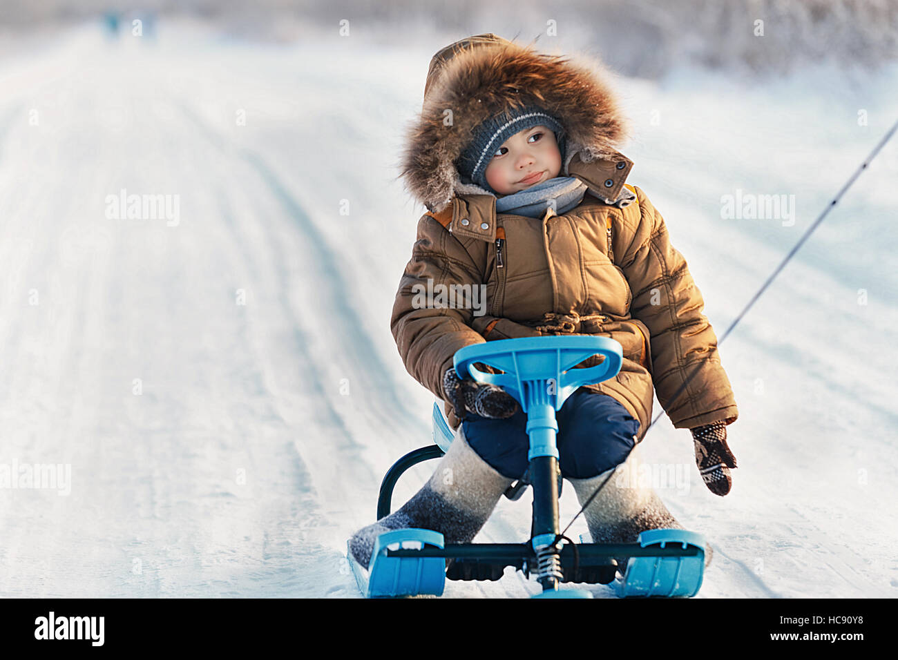 Little boy riding his kids snowmobile winter snow-covered road in the ...