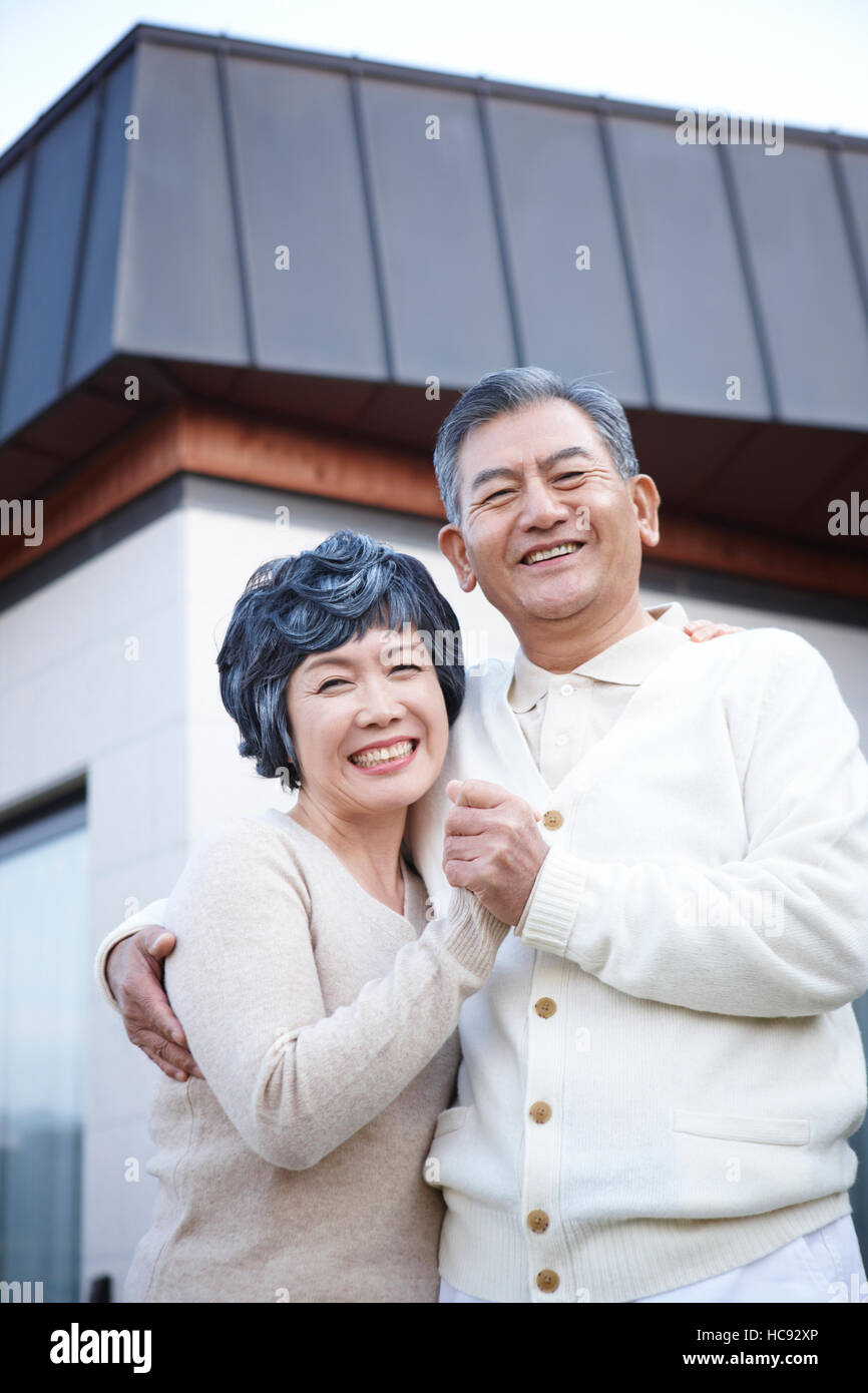 Smiling old couple hugging holding hands against house Stock Photo - Alamy
