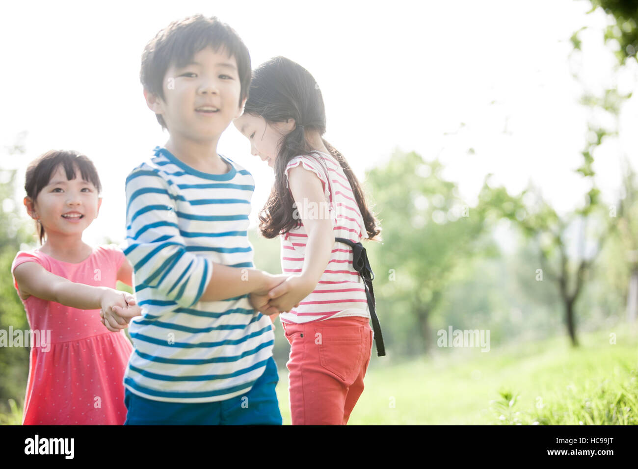 Three smiling children playing in field Stock Photo - Alamy