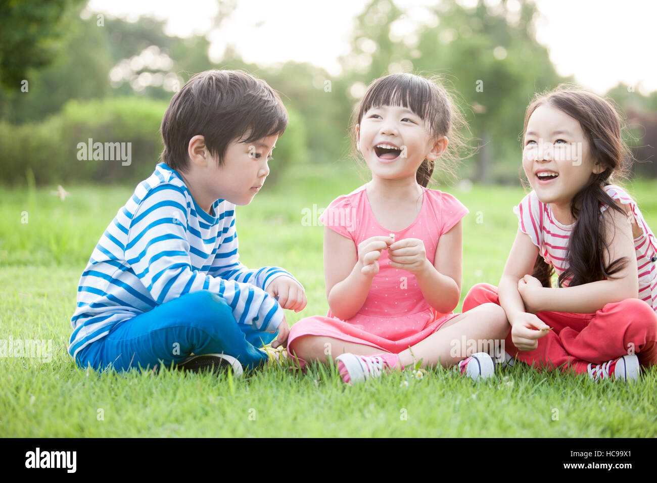 Three smiling children sitting on field Stock Photo - Alamy