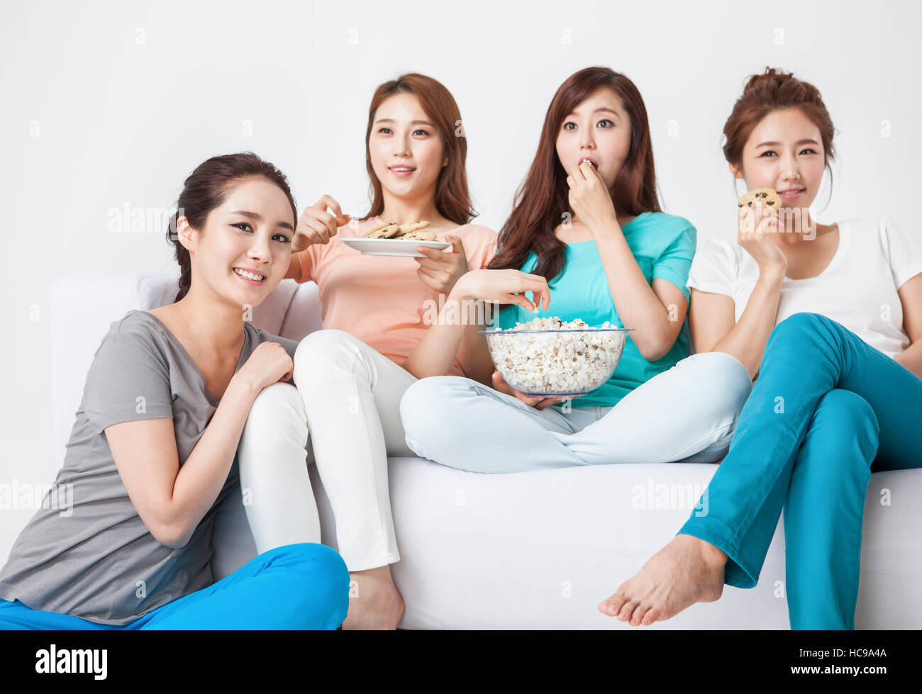 Four young women watching television eating snacks Stock Photo - Alamy