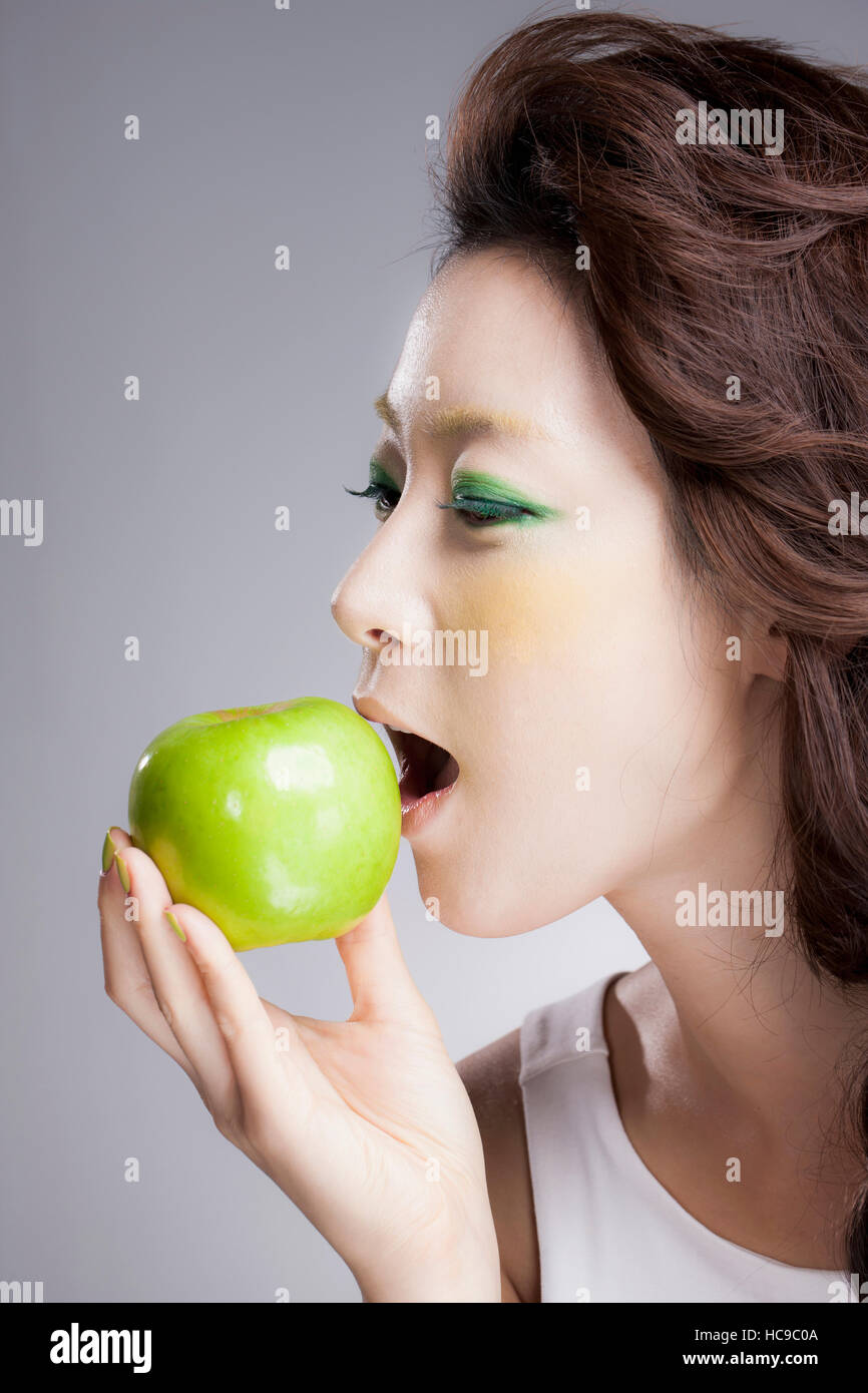 Side view of young smiling.Korean woman biting a green apple Stock ...