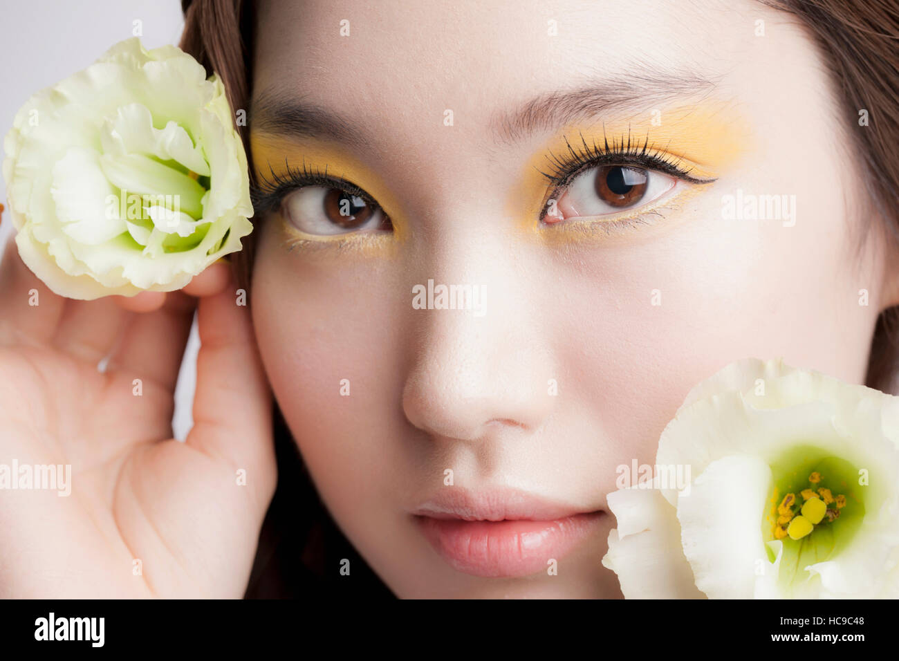Face of young Korean woman in yellow eye shadow posing with flowers ...