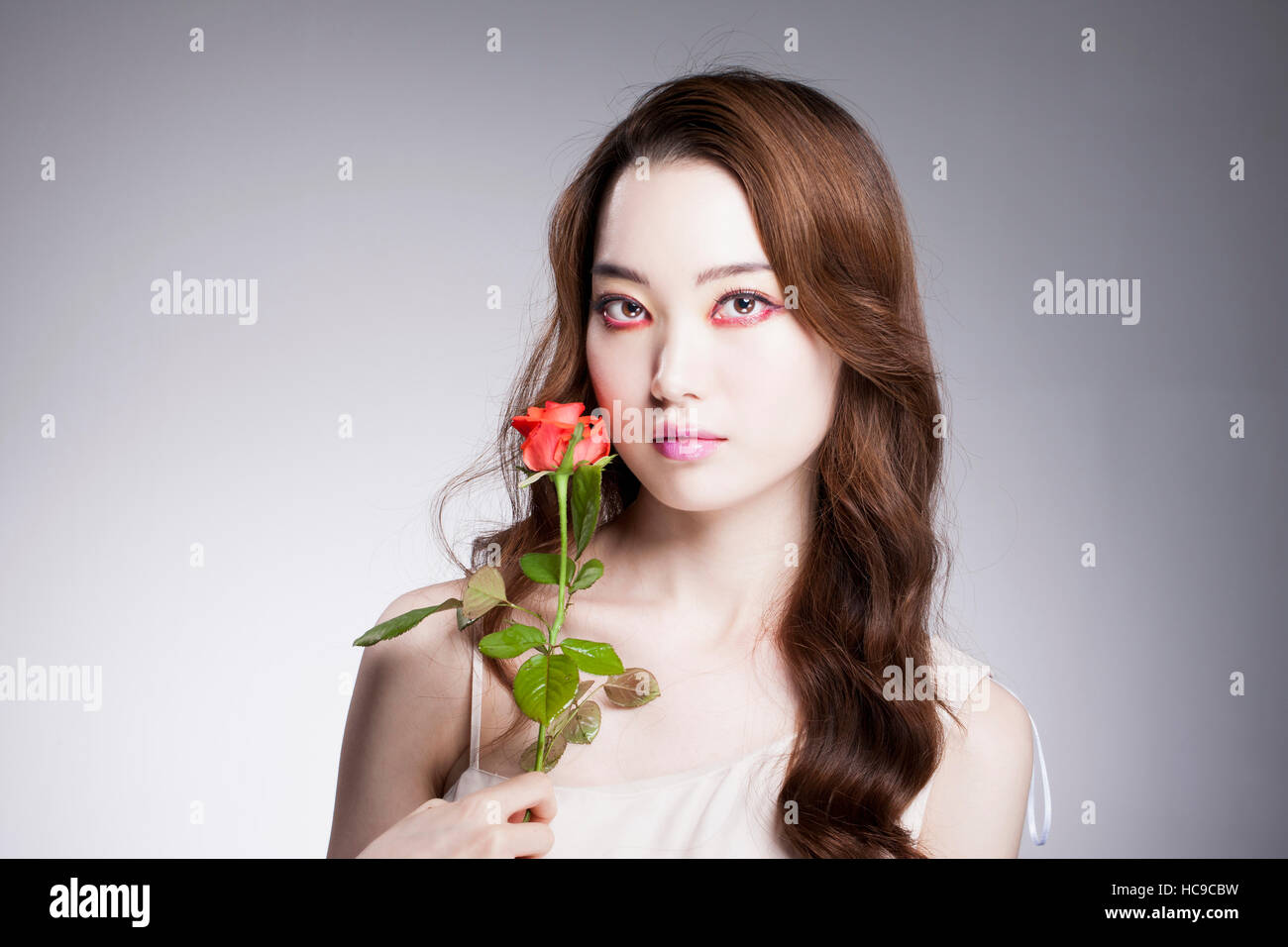 Portrait of young Korean woman in red eye liner posing with red rose ...