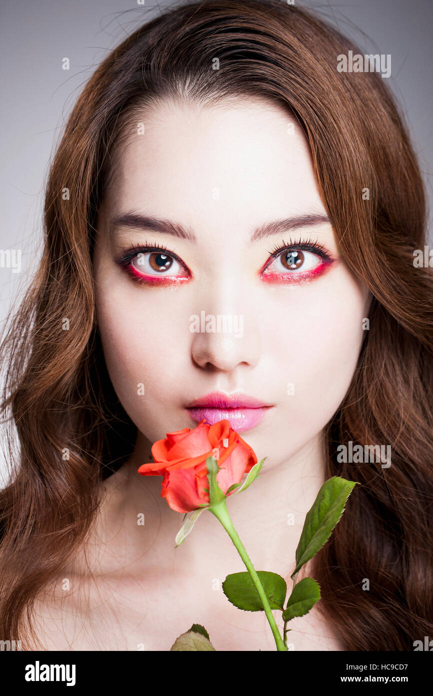 Portrait of young Korean woman in red eye liner posing with a red rose ...