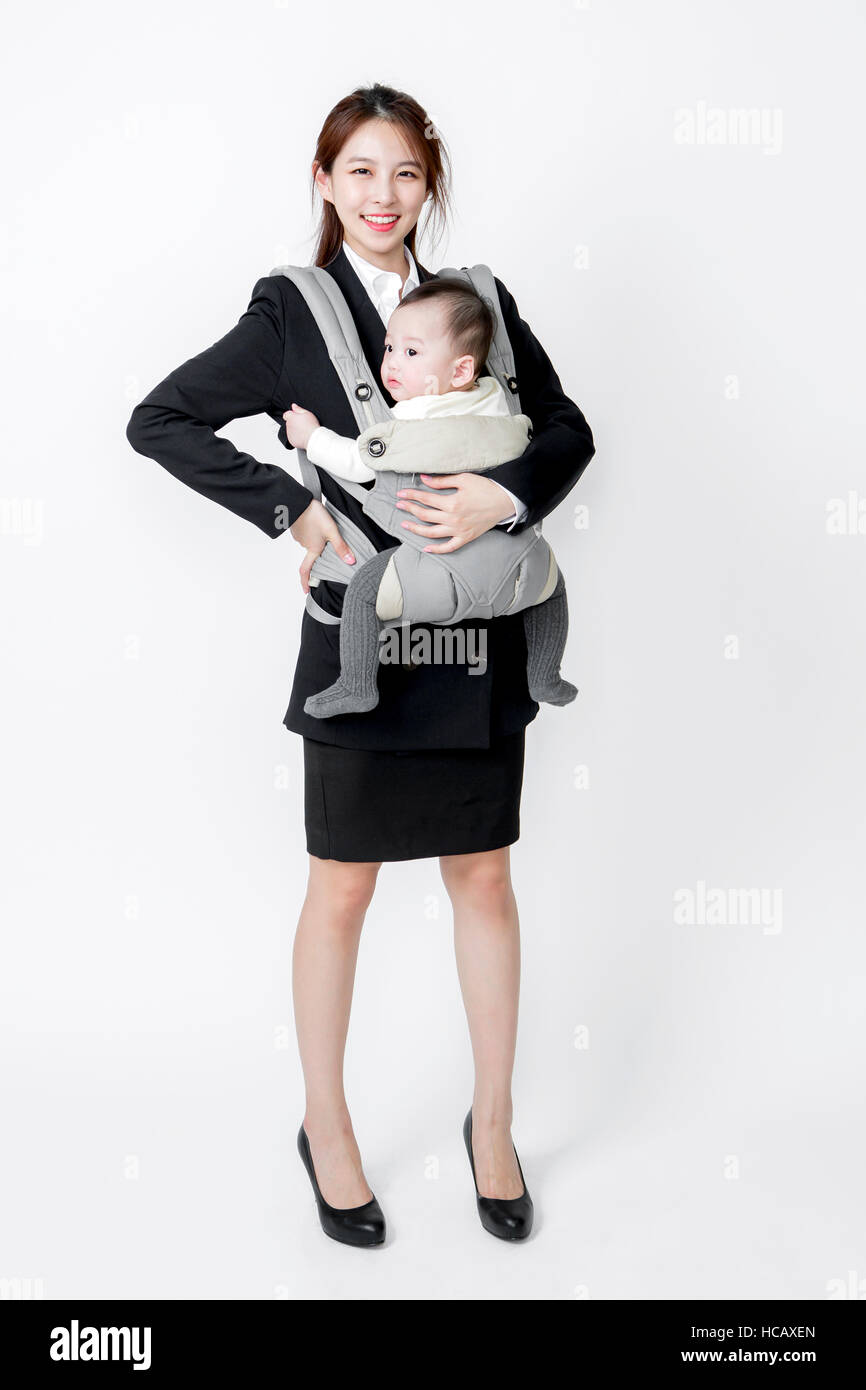 Smiling businesswoman holding her baby in a carrier standing Stock ...