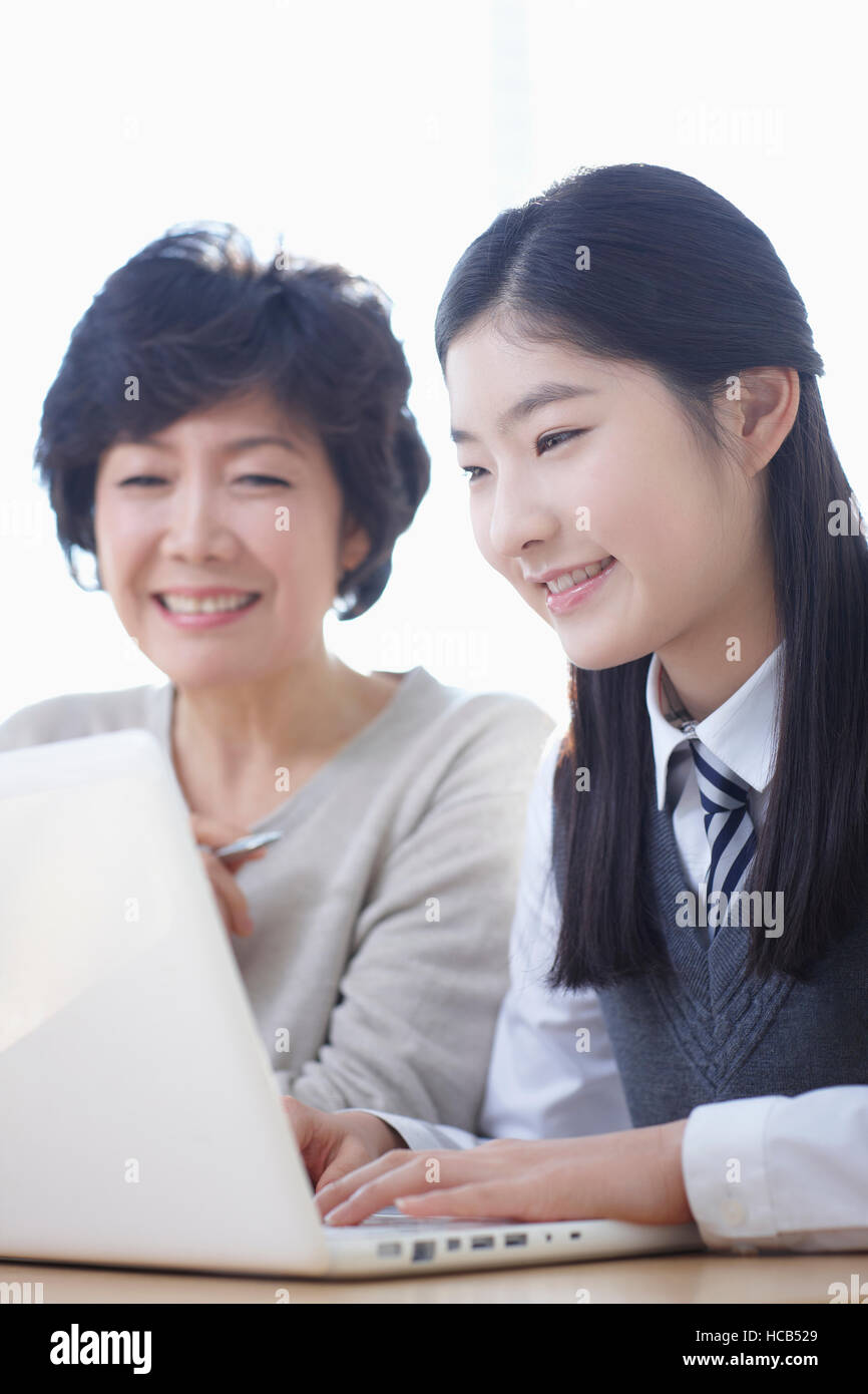 Portrait of smiling middle school girl and smiling mother using ...
