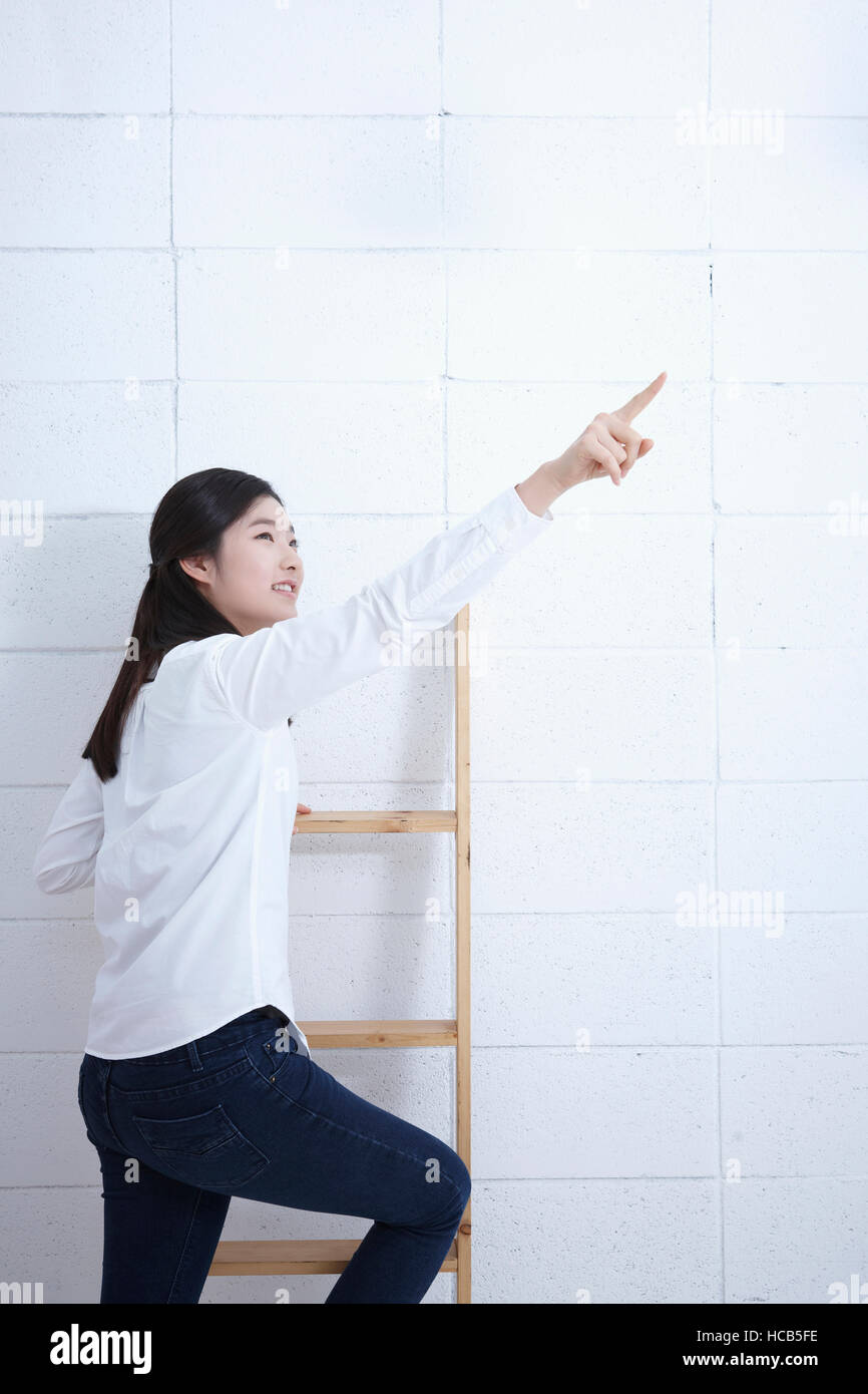 Side view of smiling adolescent girl climbing up a ladder pointing up ...