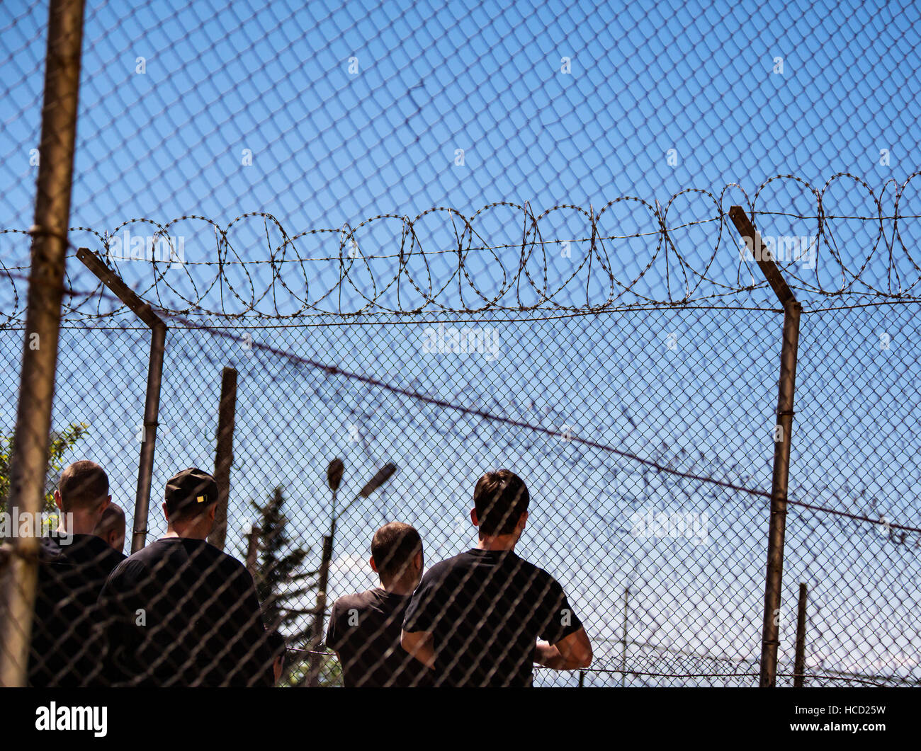High fence in refugee camp or a jail with razor wire and some people ...