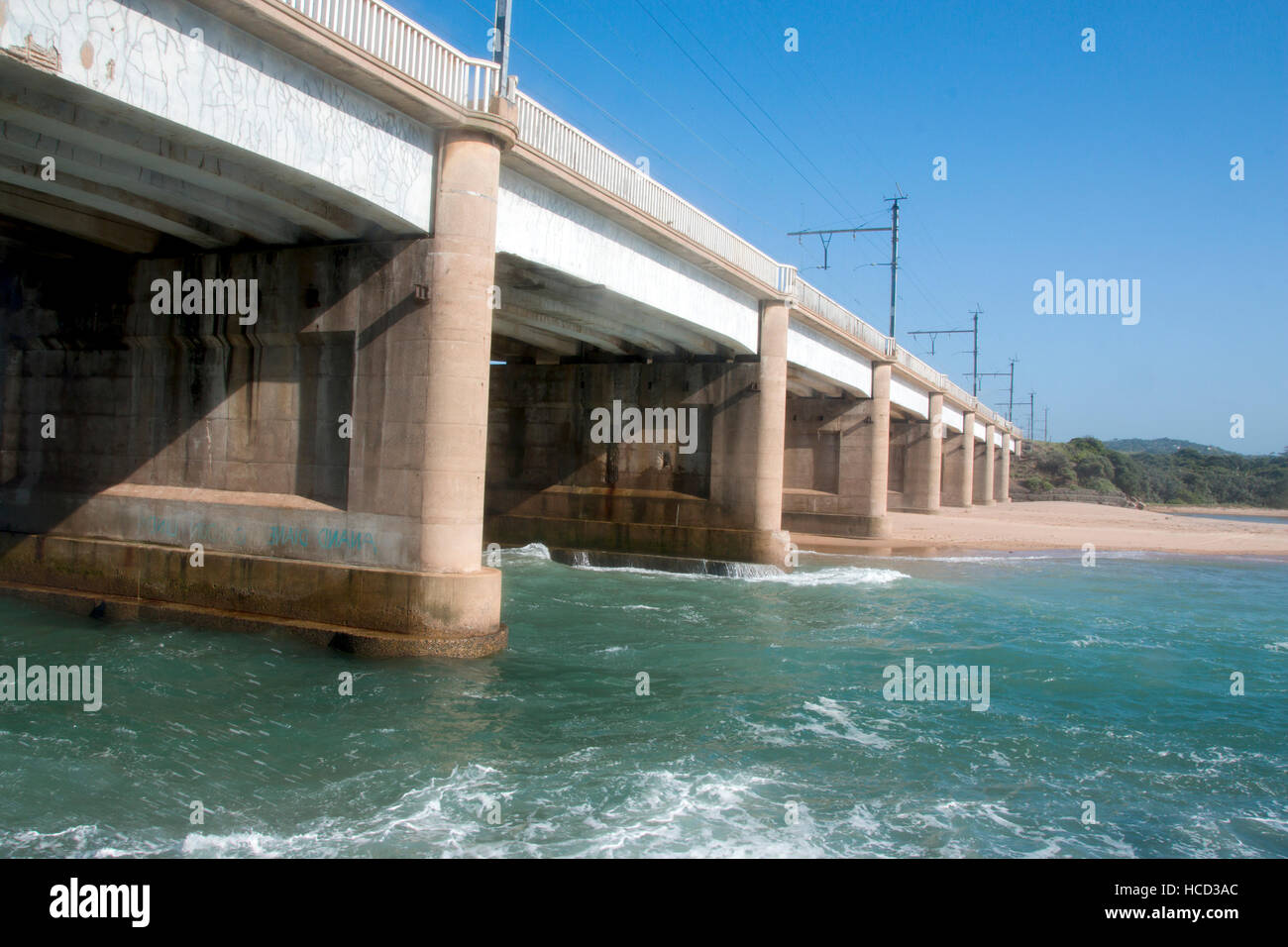 Concrete bridge extending over river mouth with incoming tide and blue ...