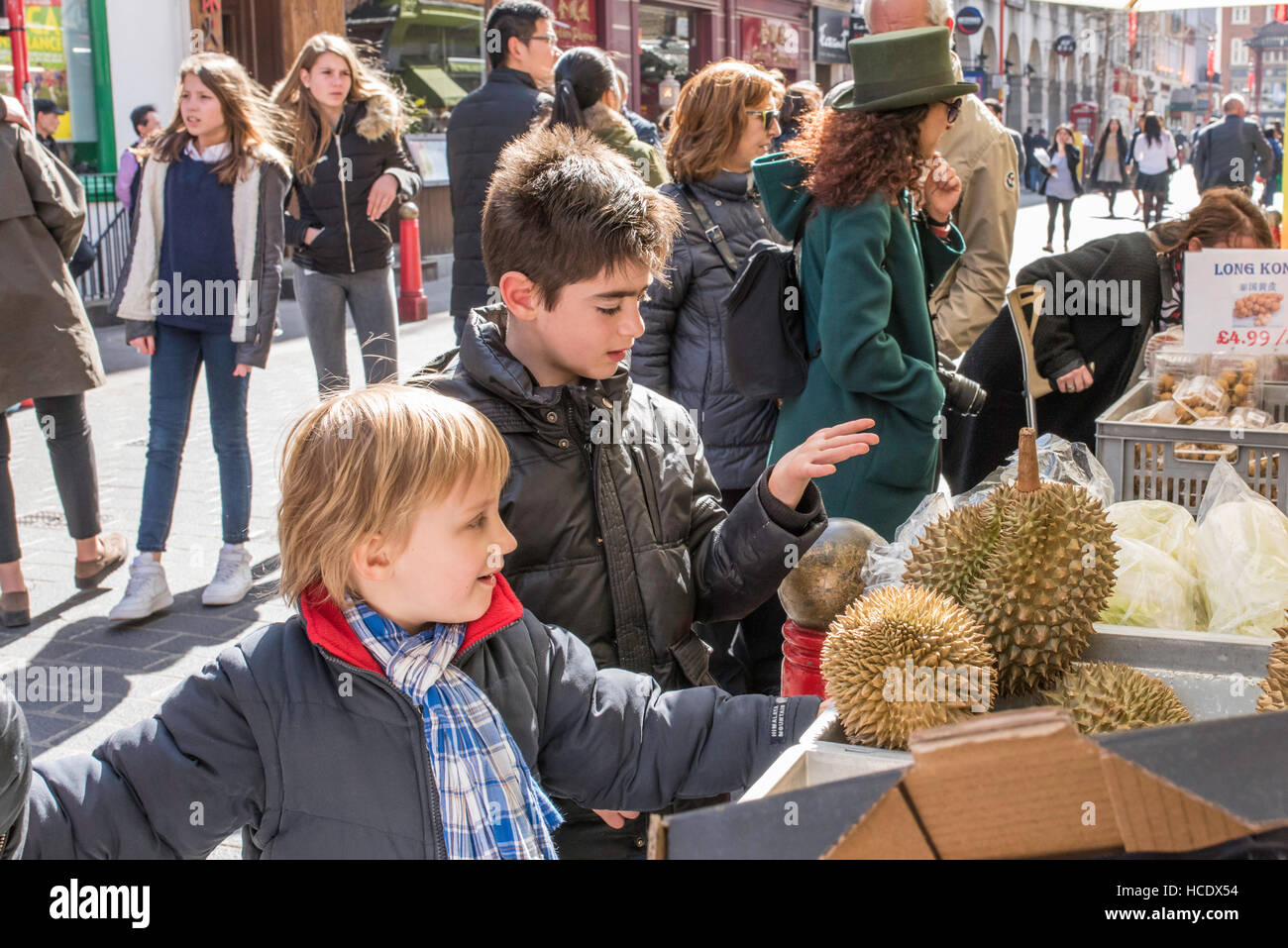 Two young boys looking and touching spiky exotic fruit on a stall at a ...