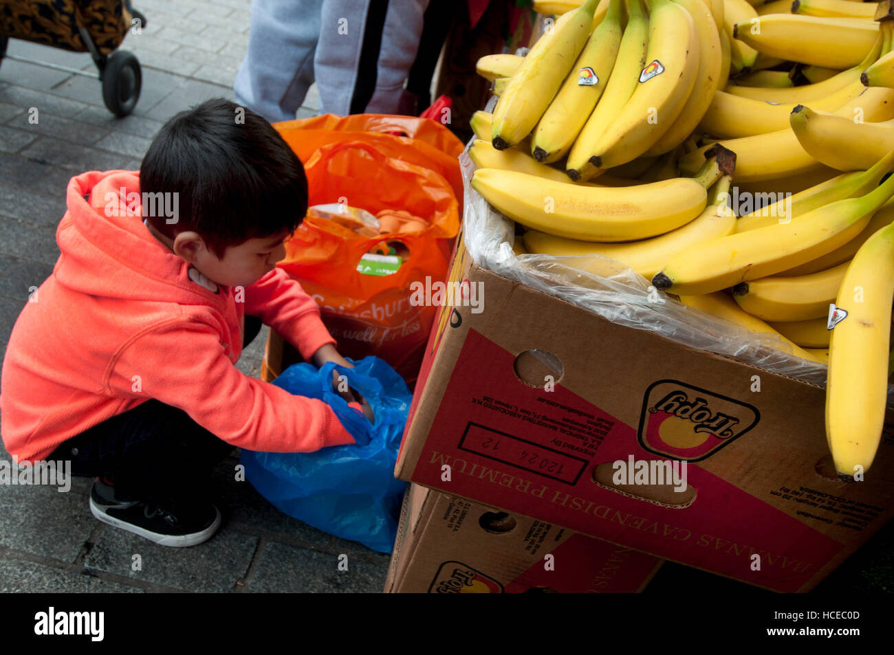 Hackney. Ridley Road market. Fruit stall. Small boy crouching and ...