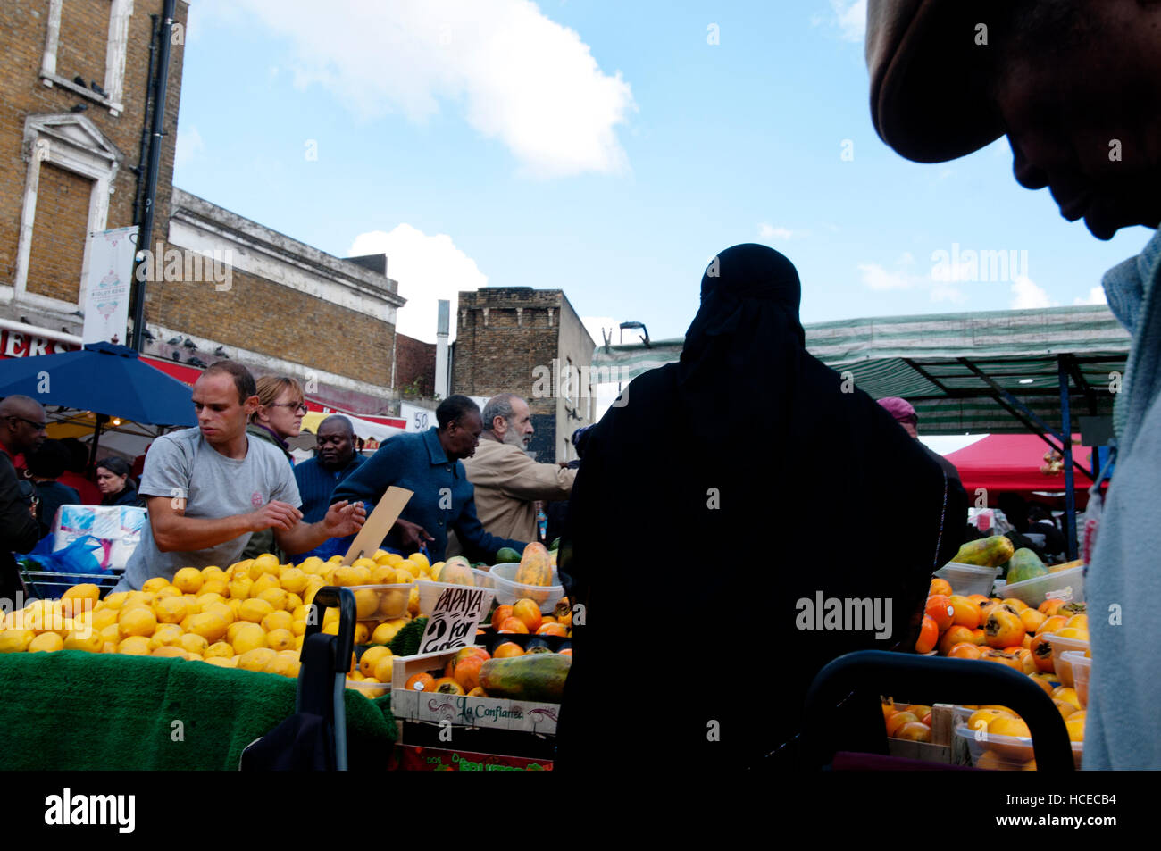 Hackney. Ridley Road market. Fruit stall. A woman wearing a full-length ...