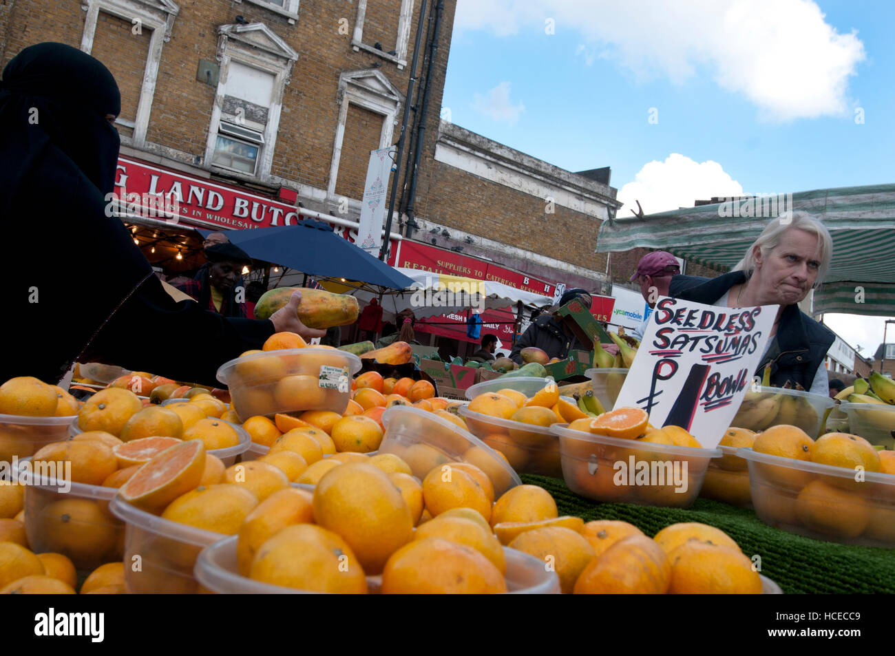 Hackney. Ridley Road market. Fruit stall. A woman wearing a full-length ...