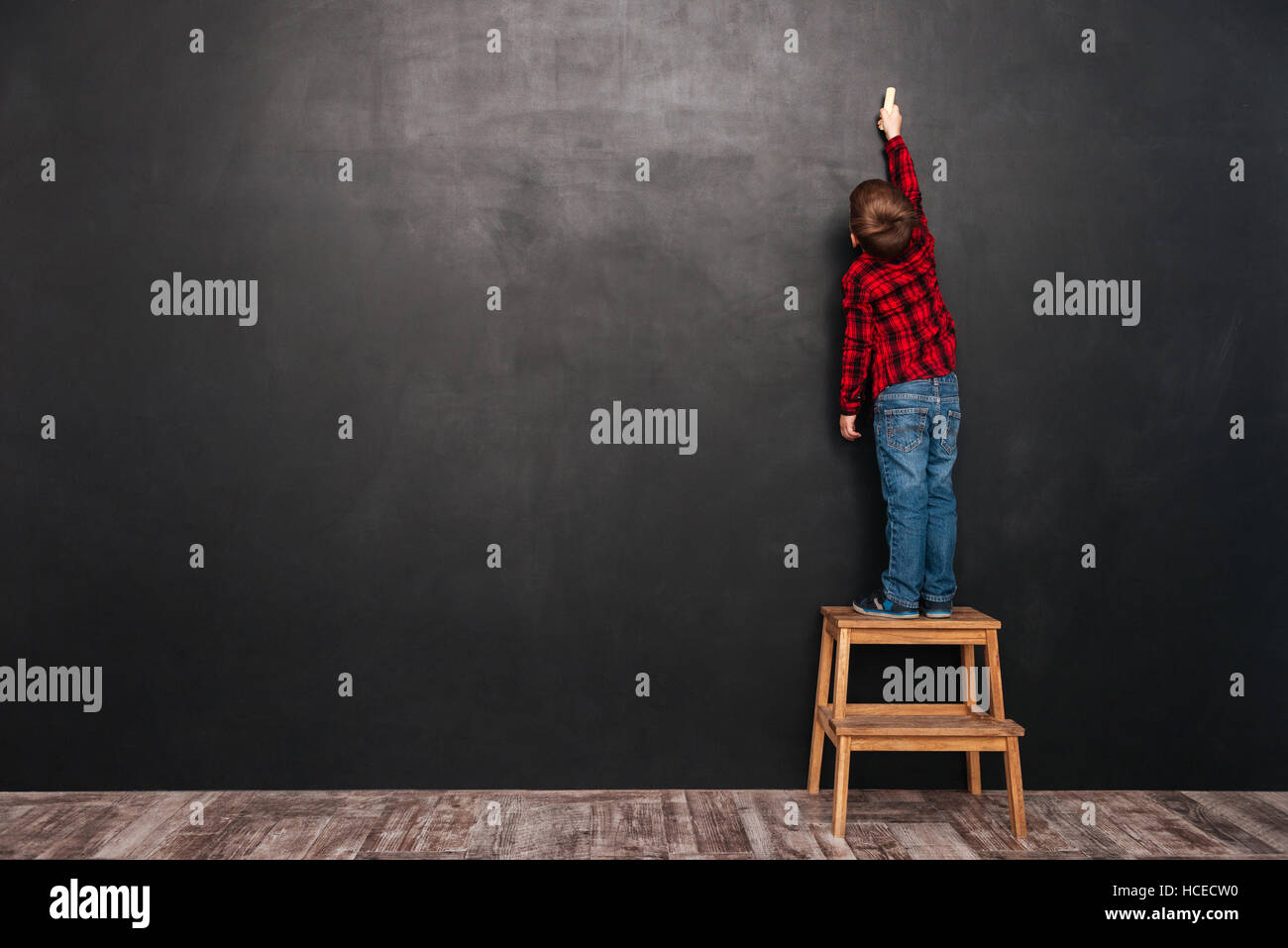 Picture of a little child standing on stool near blackboard and drawing ...