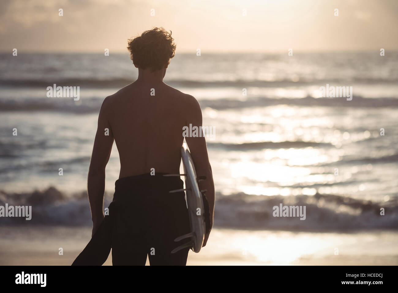 Man carrying surfboard standing on beach Stock Photo - Alamy