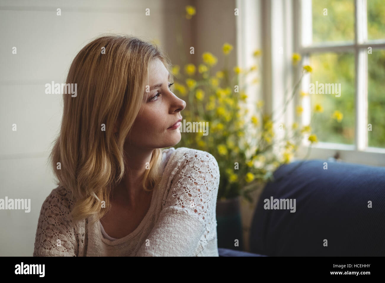Beautiful woman looking through window in living room Stock Photo - Alamy