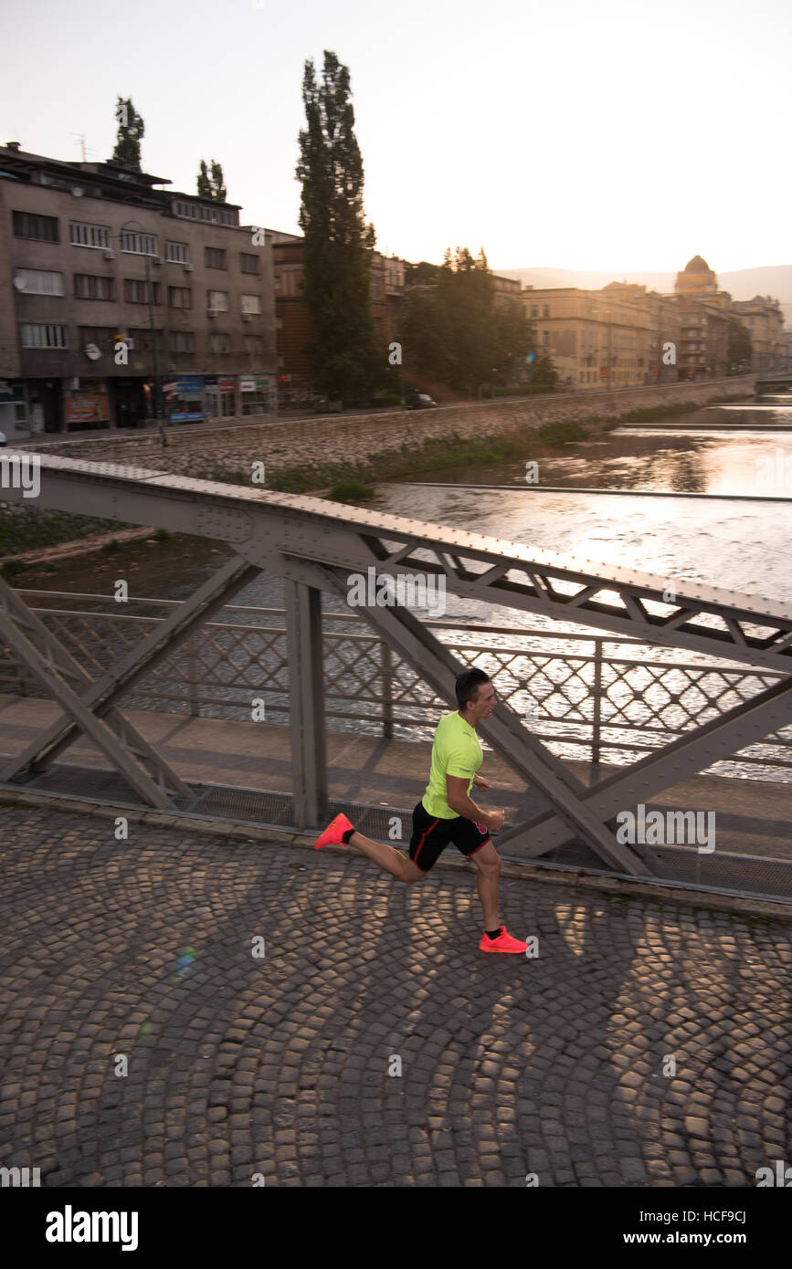 Young sporty man running on sidewalk at early morning jogging with city ...