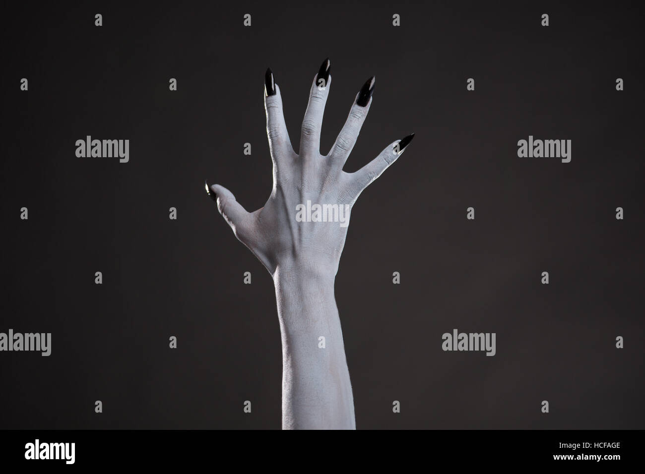 Spooky white hand with black nails, studio shot on black background ...