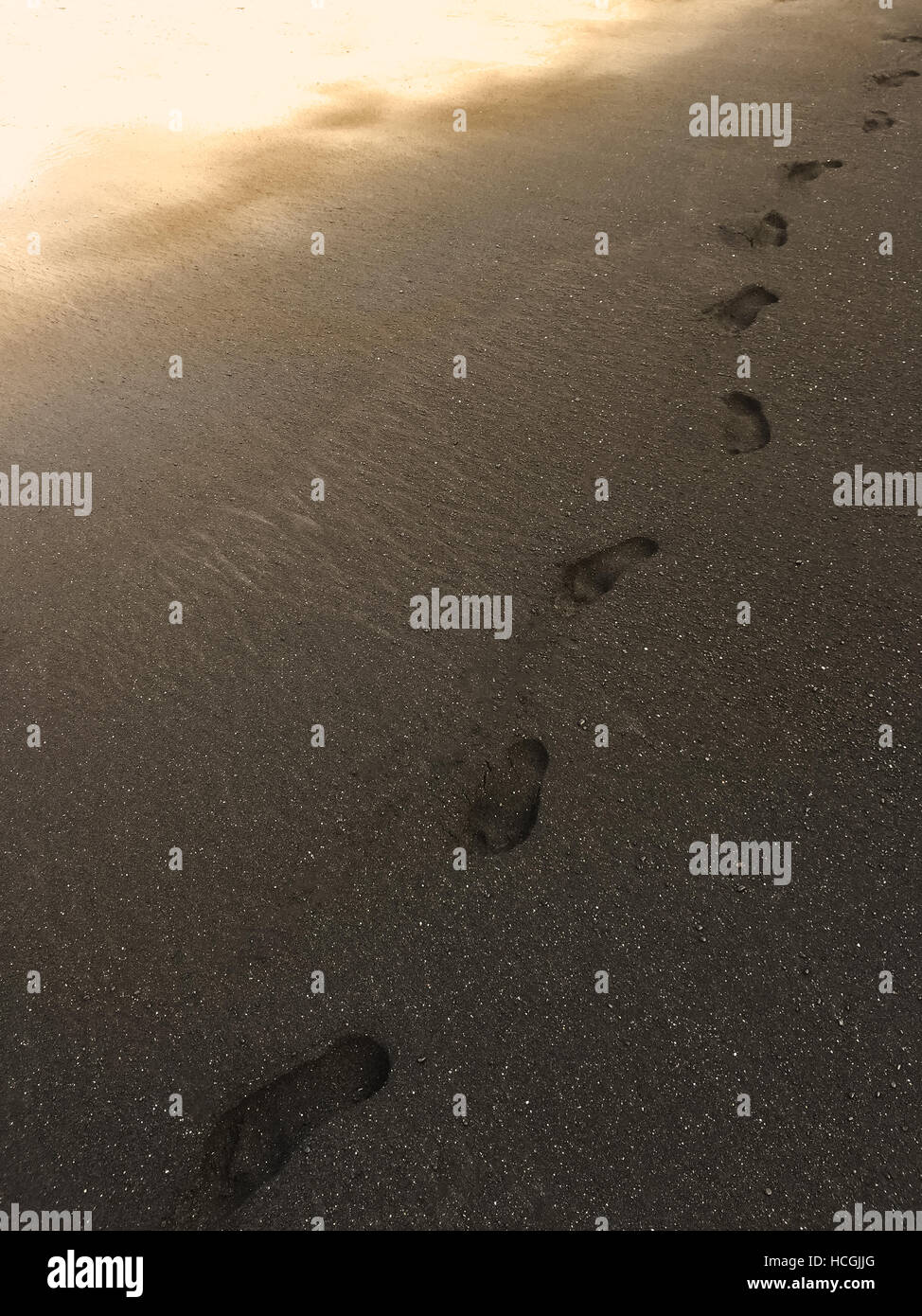 Footprints after lone walk on black sand beach by the ocean - maui ...