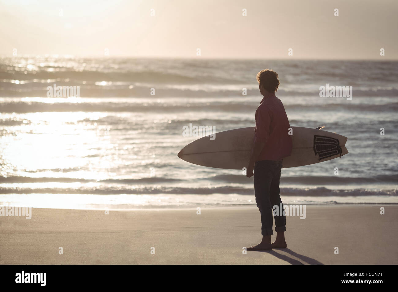 Man carrying surfboard standing on beach Stock Photo - Alamy
