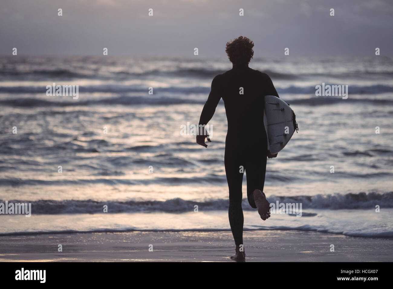Man carrying surfboard running towards sea Stock Photo - Alamy