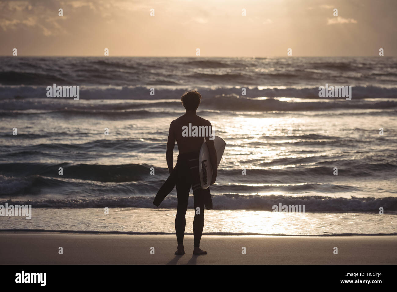 Man carrying surfboard standing on beach Stock Photo - Alamy