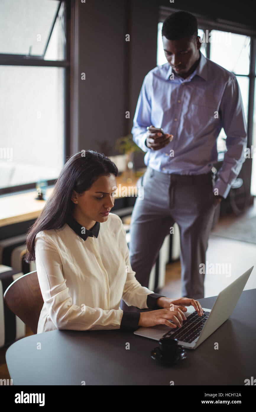 Businesswoman working on laptop while man using mobile phone Stock ...