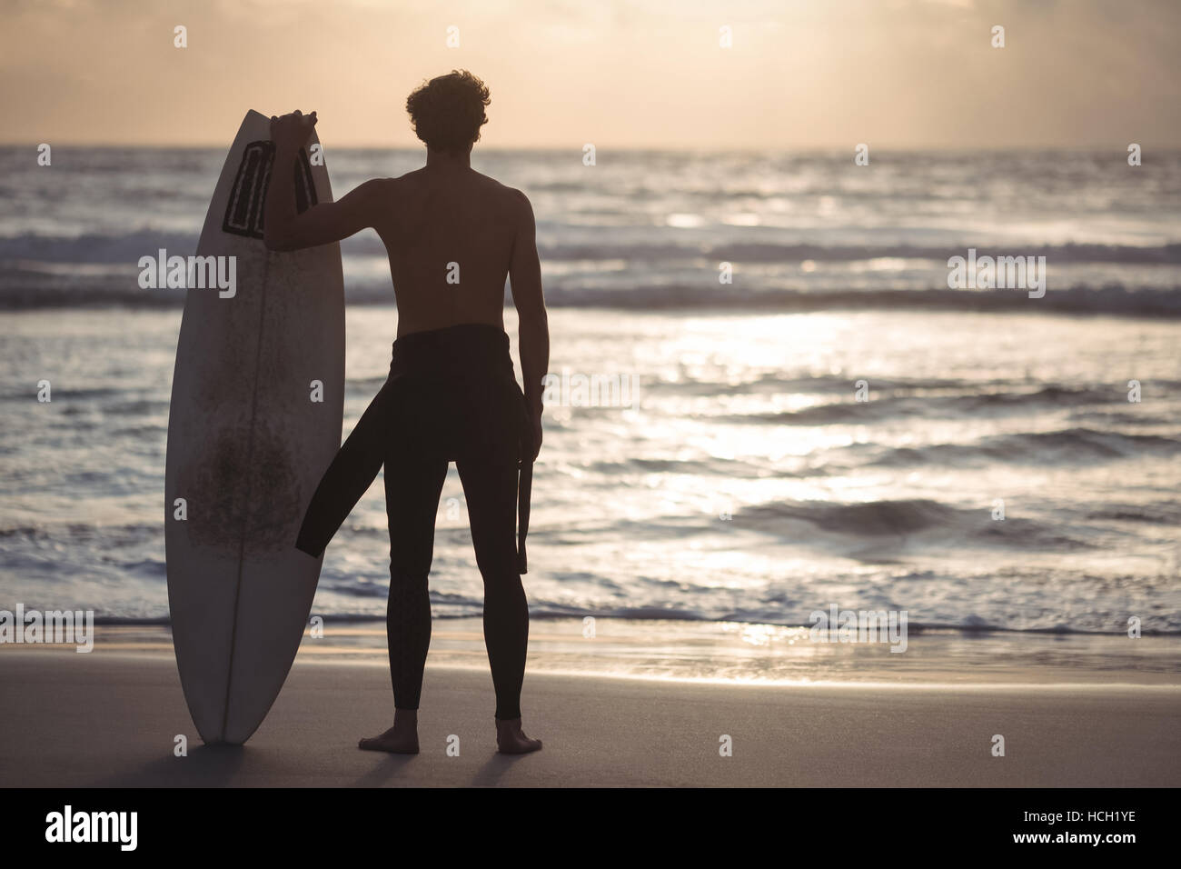 Man carrying surfboard standing on beach Stock Photo - Alamy