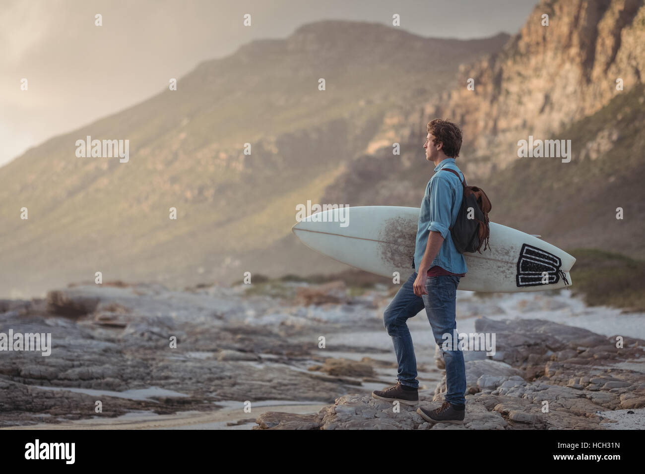 Man carrying a surfboard standing by sea Stock Photo - Alamy