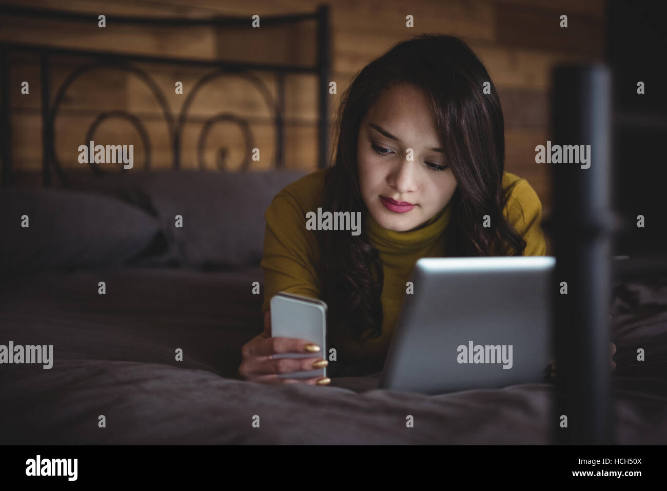 Woman lying on bed using digital tablet and mobile phone in bedroom ...