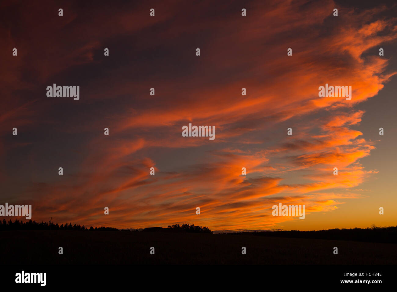 Angled red, orange, and yellow clouds at sunset over a silhouetted ...