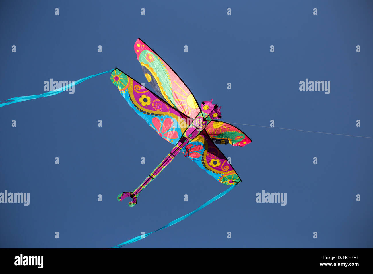 Colorful dragonfly kite with blue tails and a string flying in a blue ...