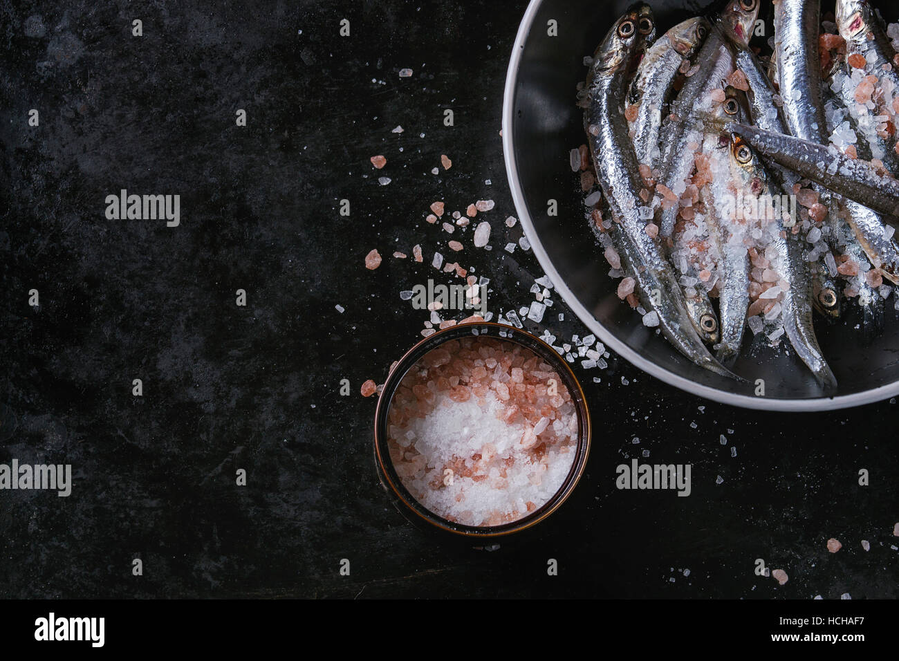Lot of raw fresh anchovies fishes in black ceramic bowl with pink and ...