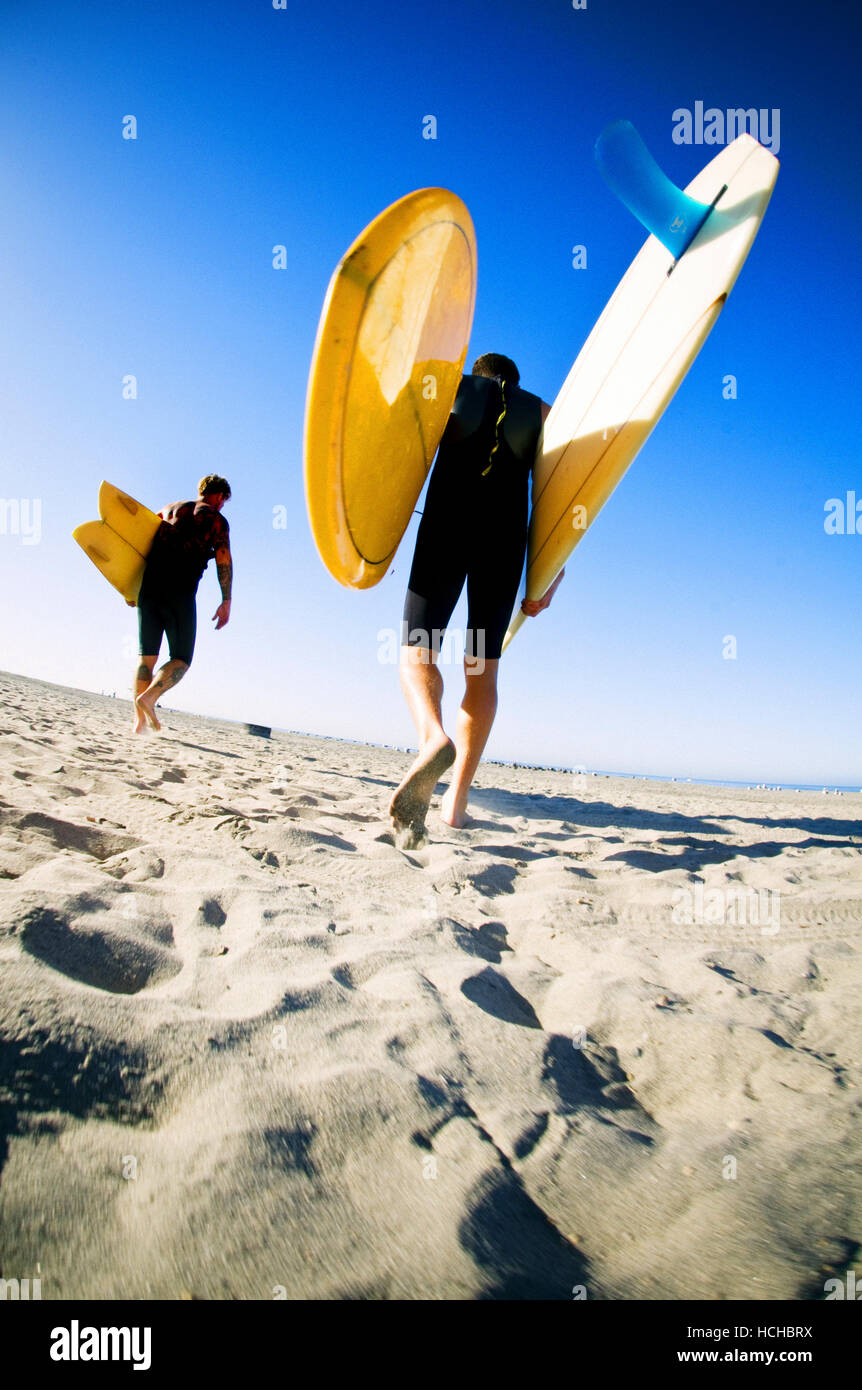 Early morning sun shines on two young men carrying surfboards on the ...