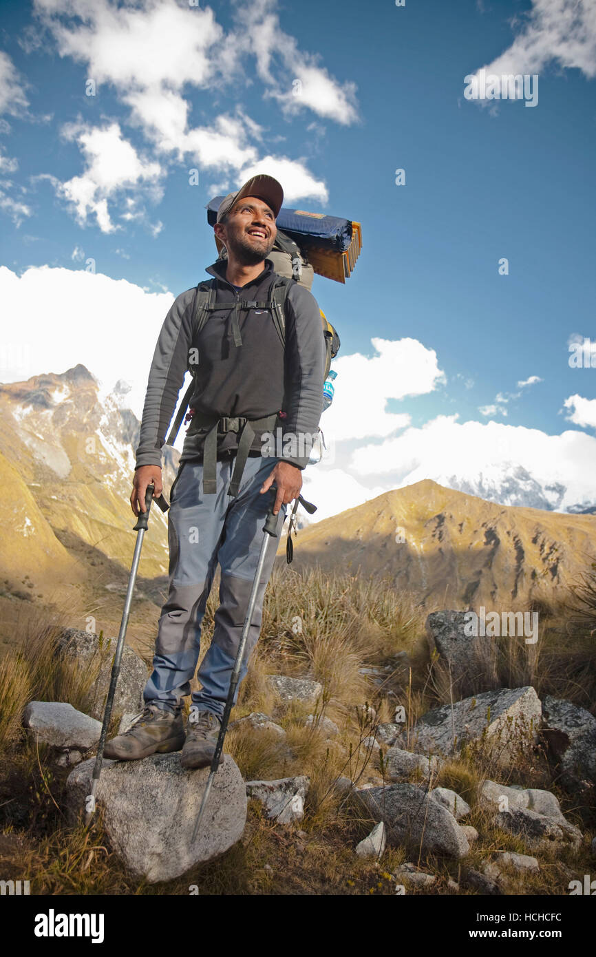 A man with trekking poles stands on a rock during his trek to Pisco ...