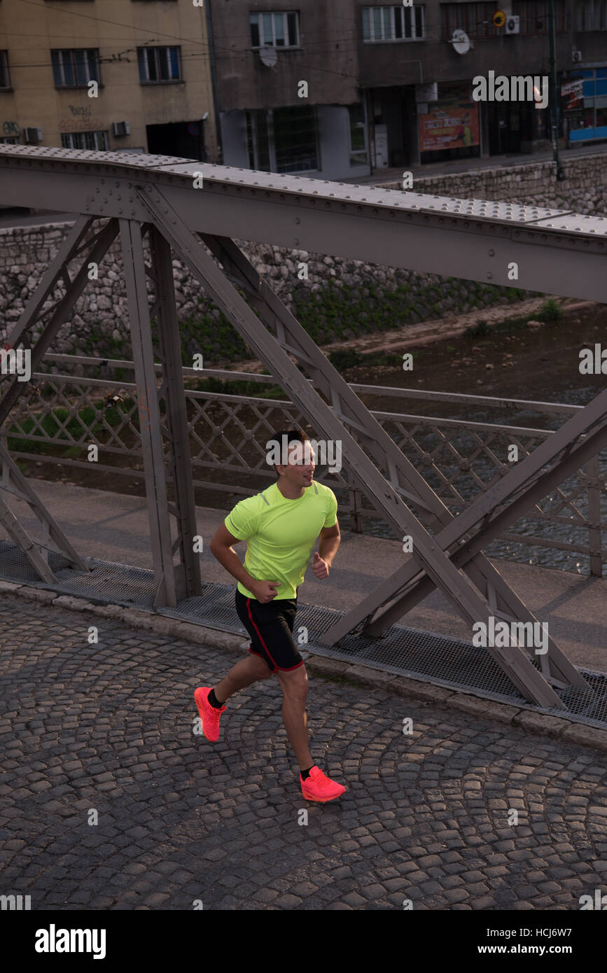 Young sporty man running on sidewalk at early morning jogging with city ...