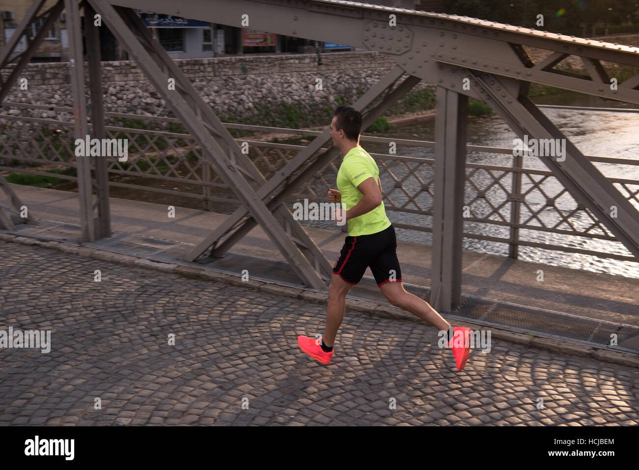 Young sporty man running on sidewalk at early morning jogging with city ...