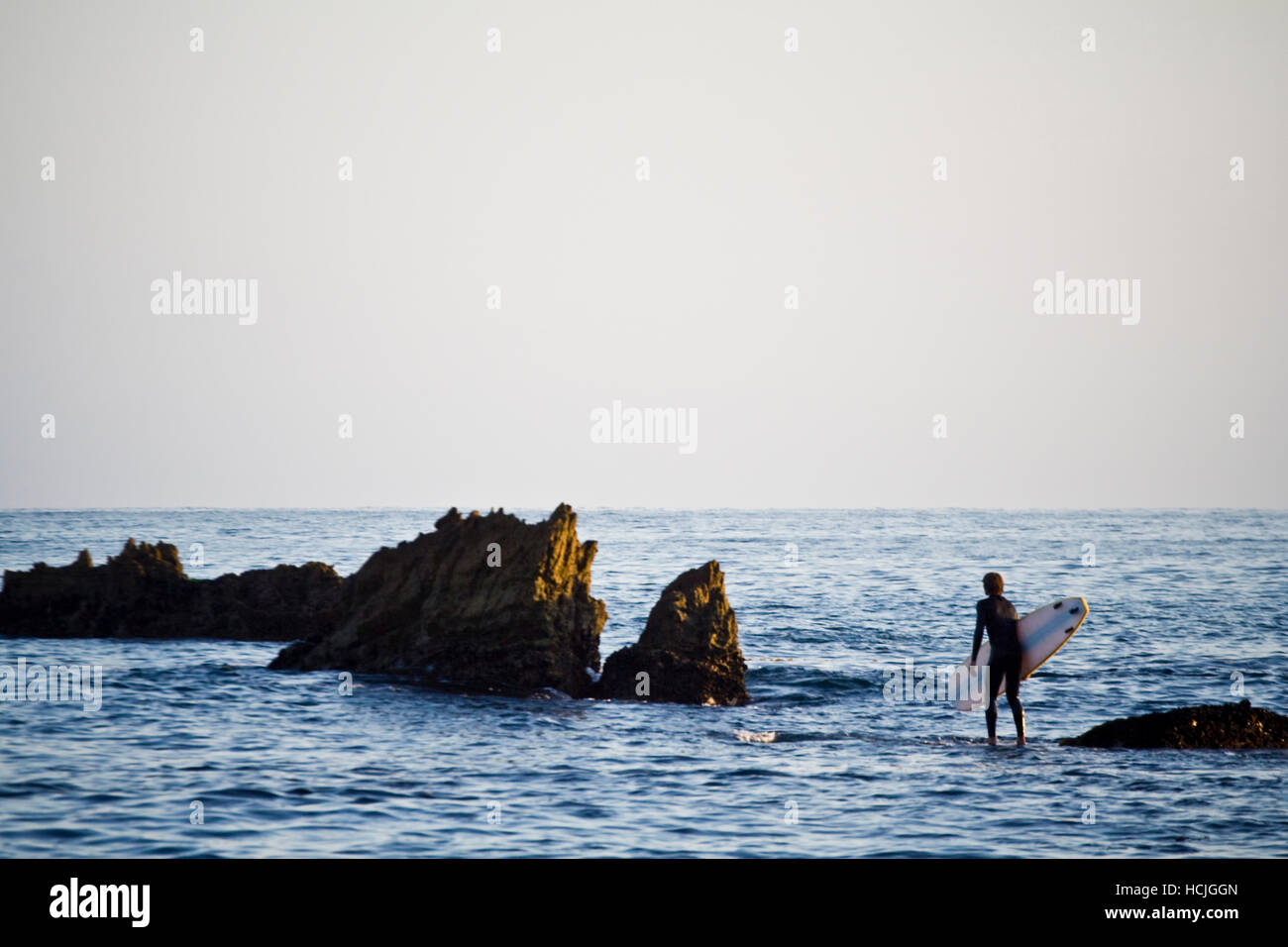A surfer stands up with his surfboard on a rock outcrop off of Laguna ...