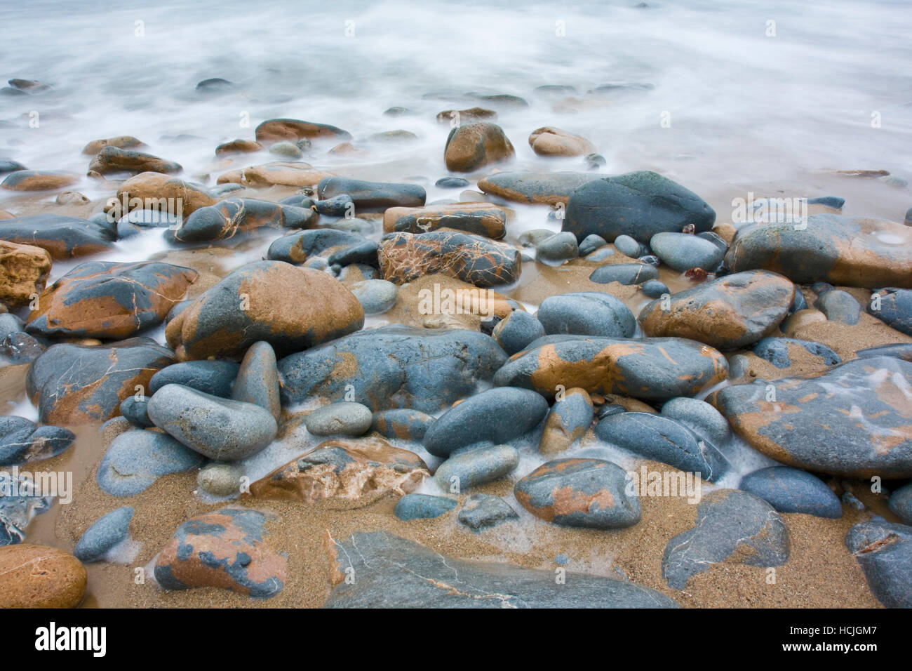 Waves swirl over colorful rounded rocks on the rocky shore of Pescadero ...