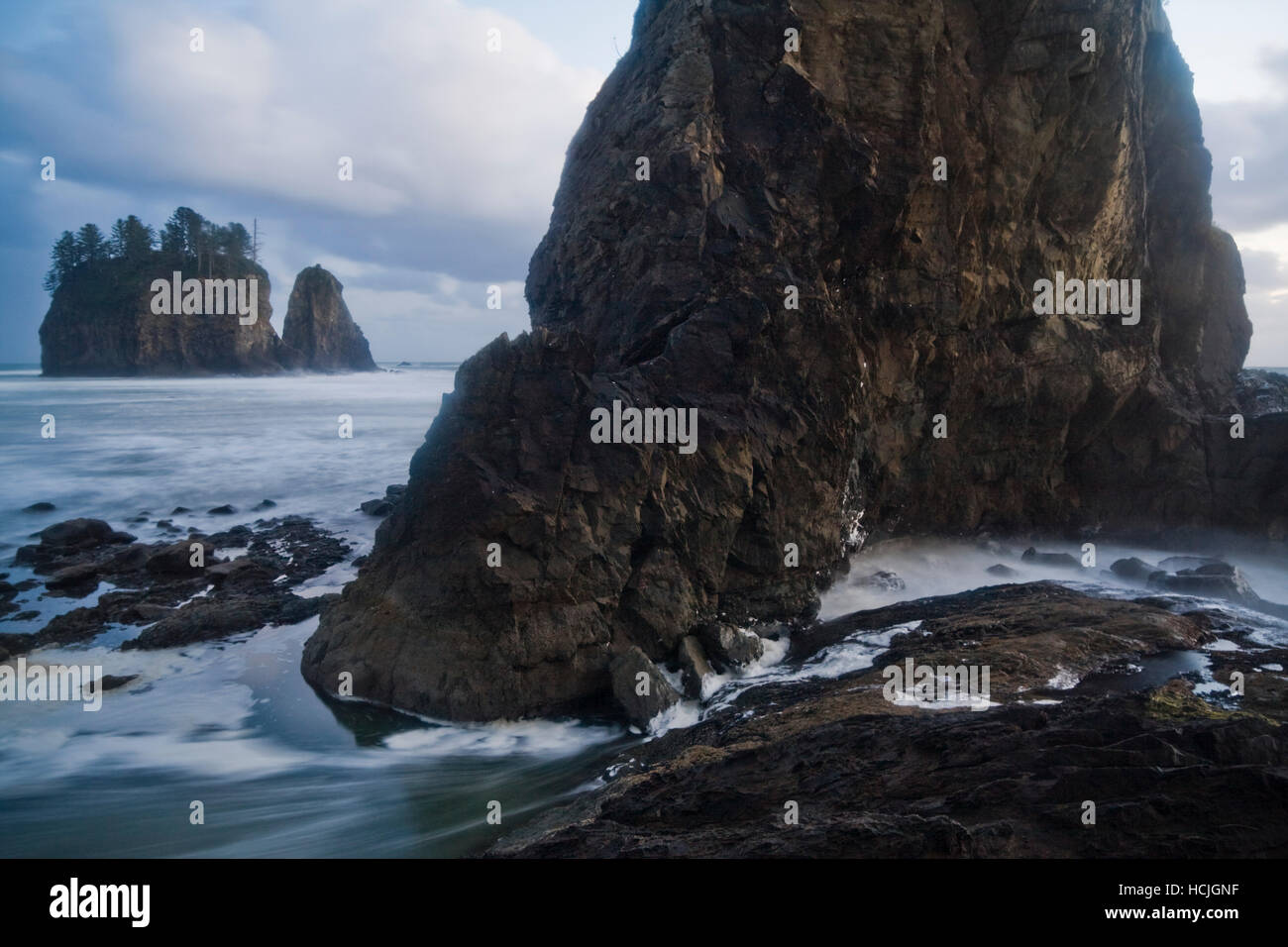 Waves pour through a gap in the rocky shore, among large sea stacks, at ...