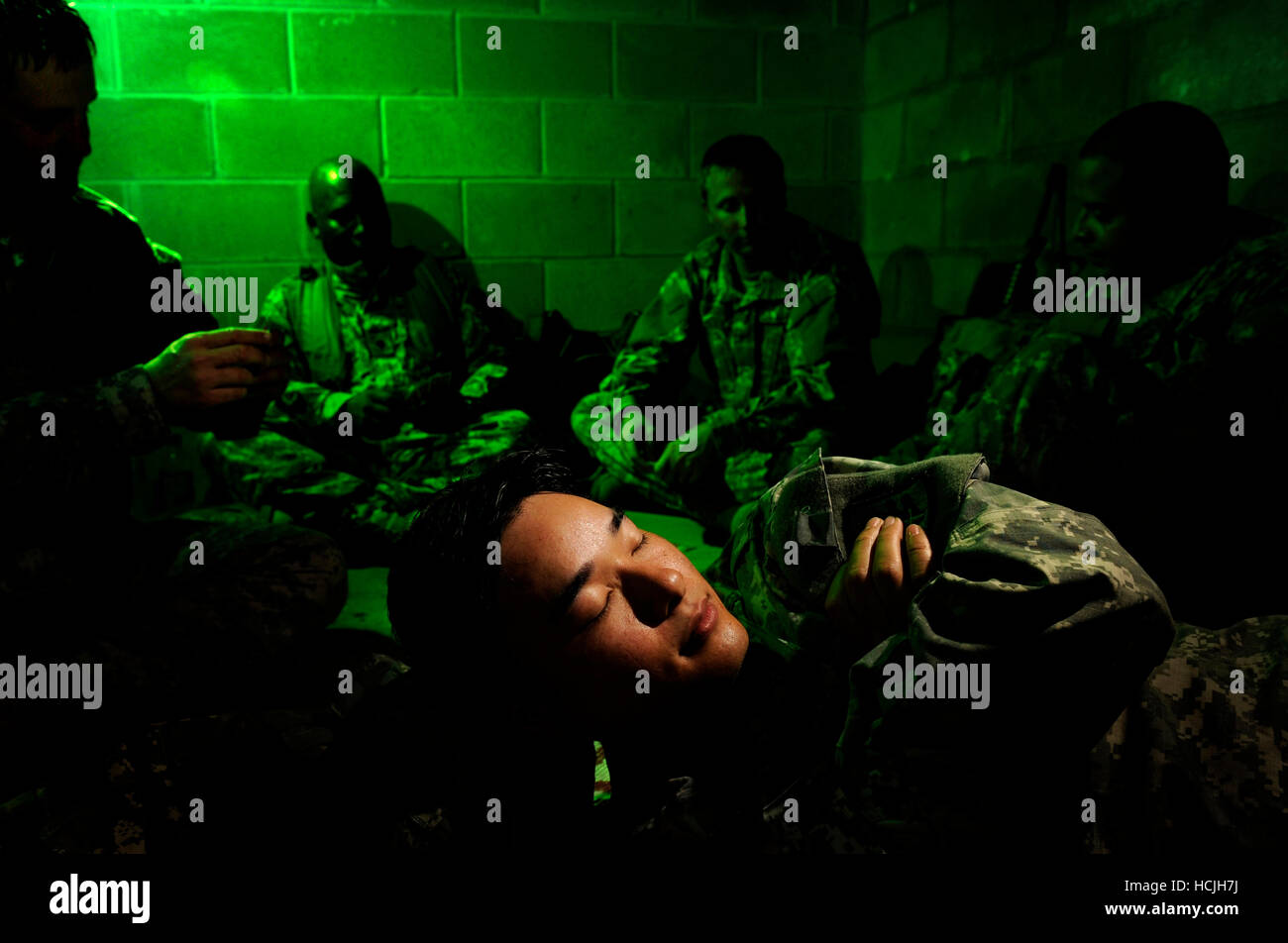 A soldier sleeps in a dark basement with very little light. Other ...