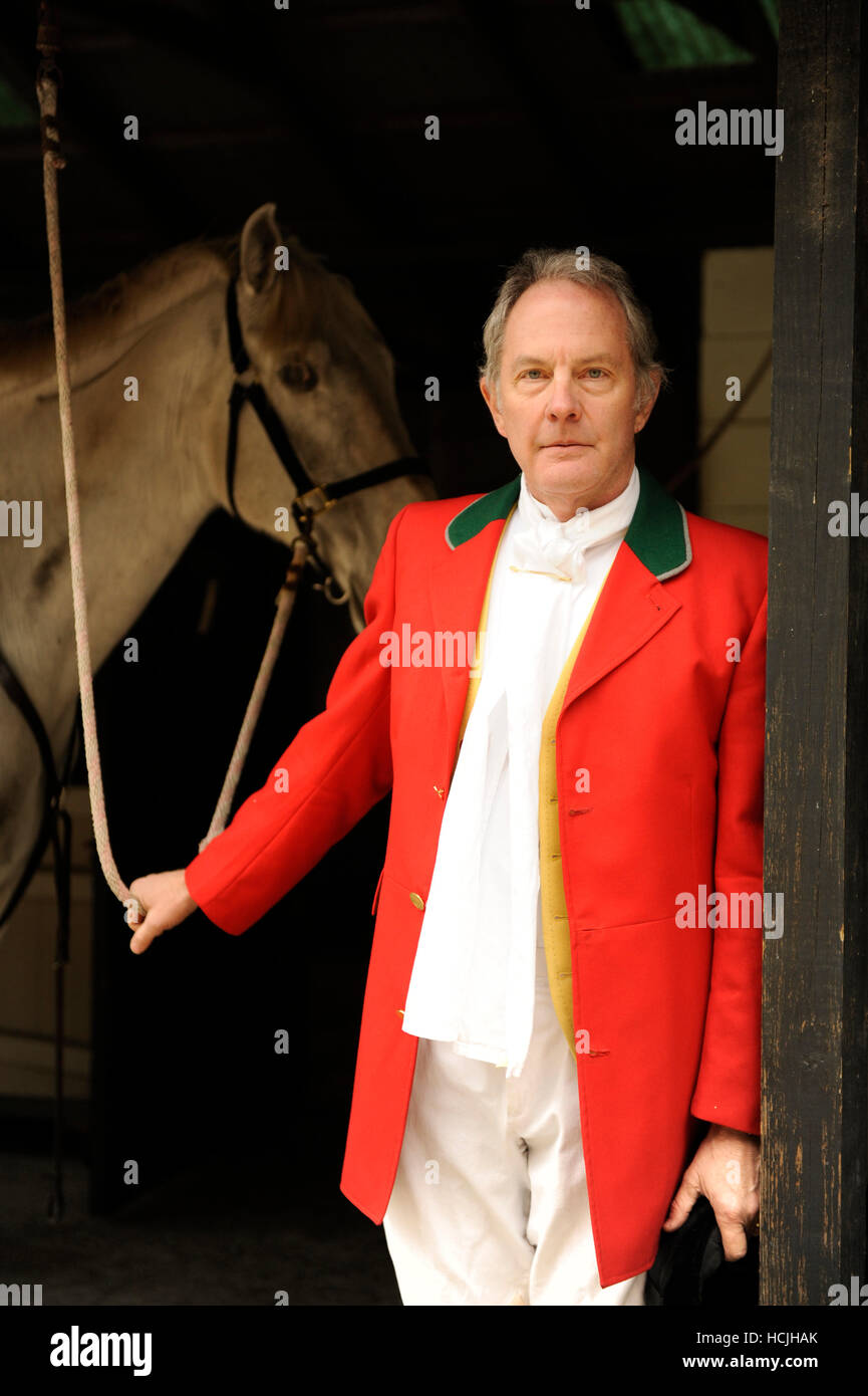 The hunt master stands near his horse while wearing his traditional red ...